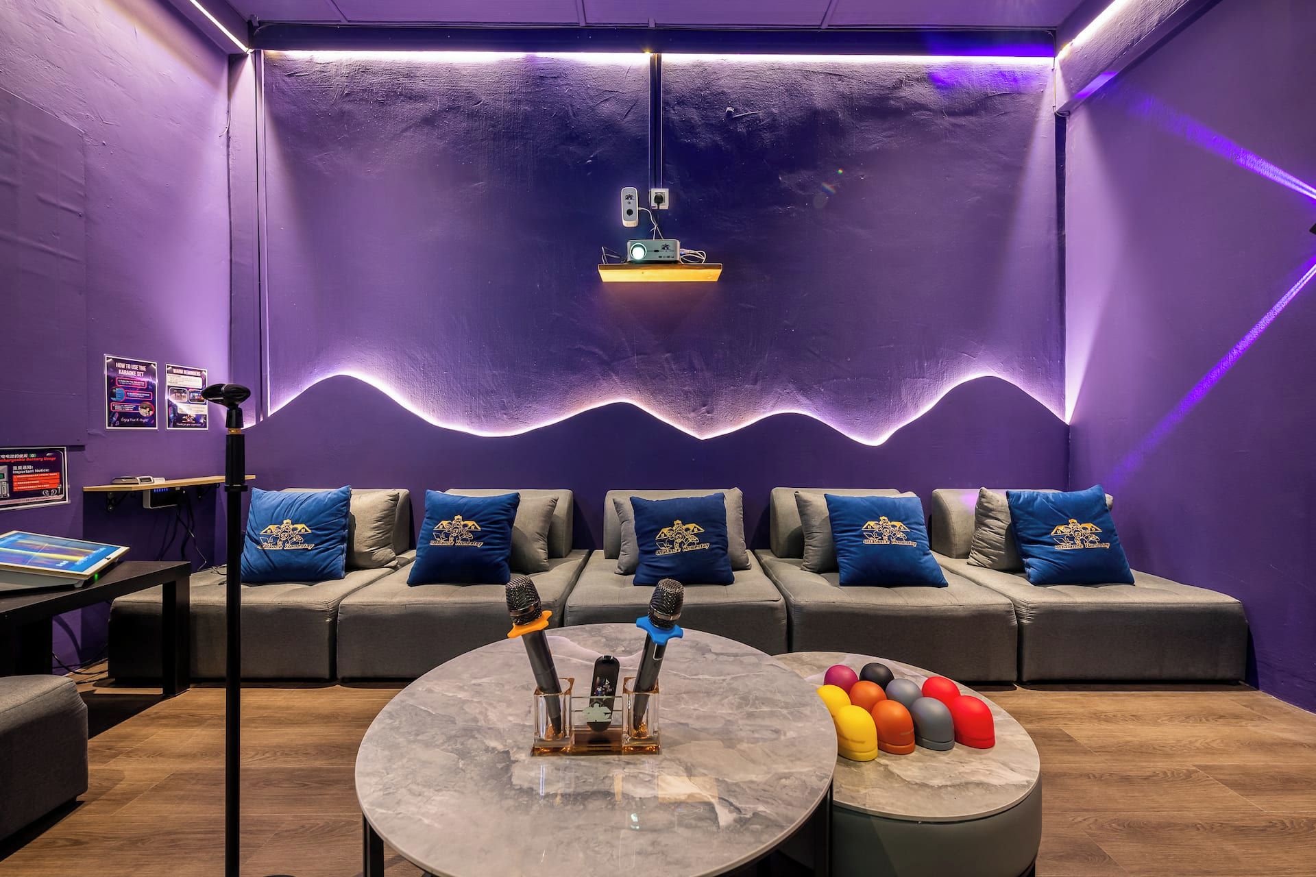 Quarto em tons de roxo, com área de estar, mesa e suporte para microfone, e um projetor fixado na parede.