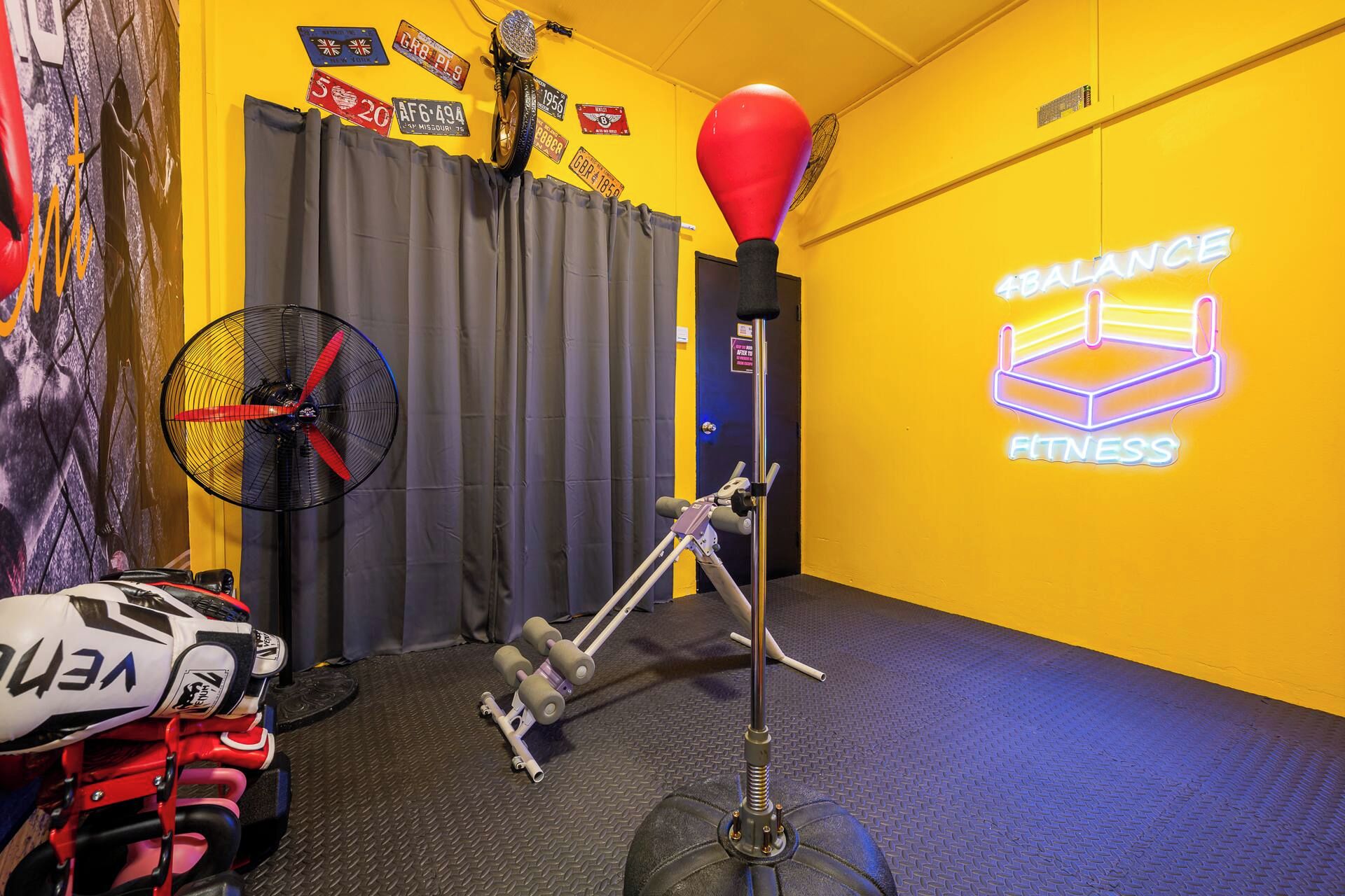 Academia com saco de pancadas, equipamentos de ginástica e um letreiro de neon com a inscrição '4BALANCE FITNESS'.