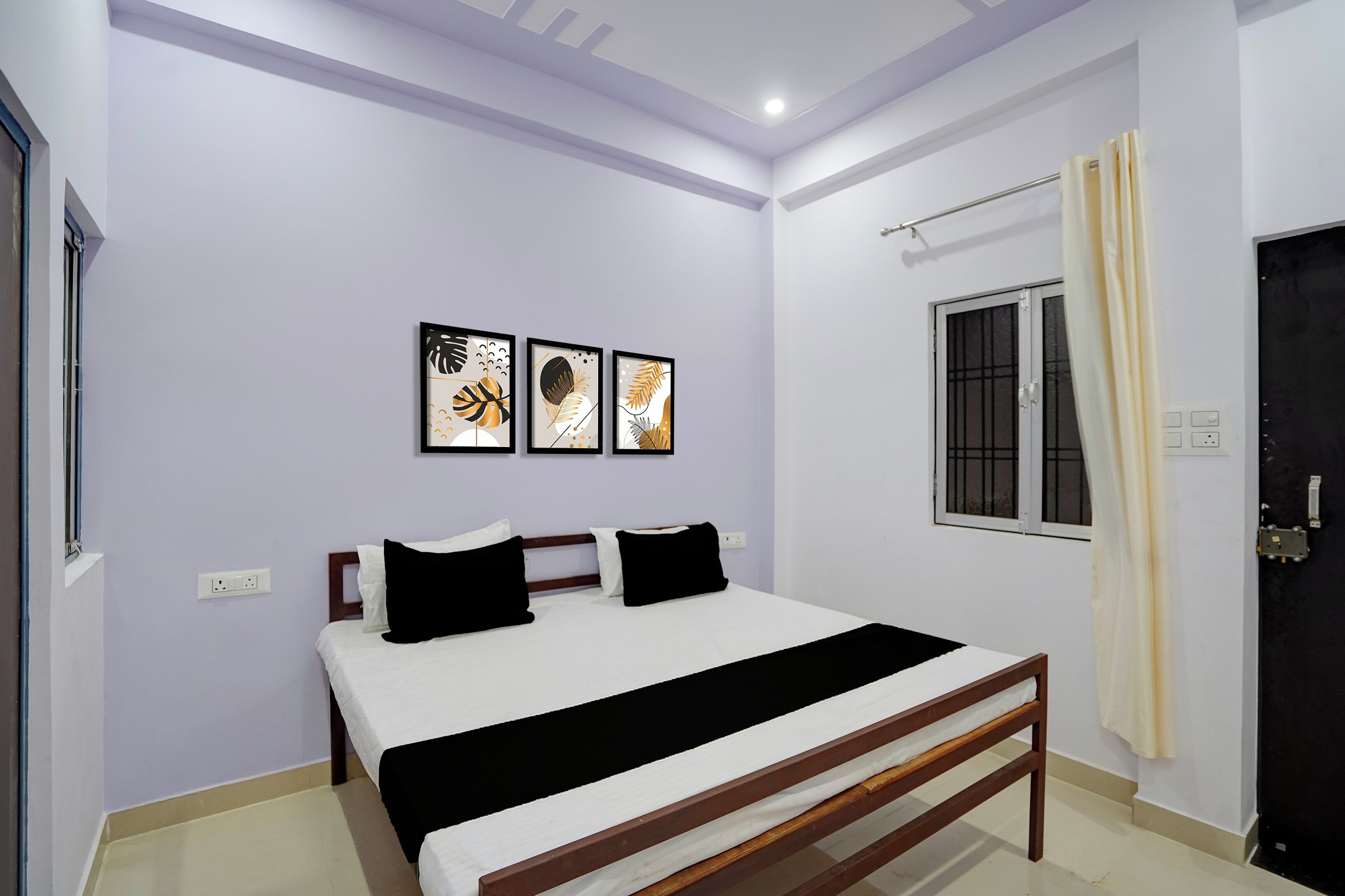 Quarto com cama, janela com cortina e três obras de arte emolduradas na parede.
