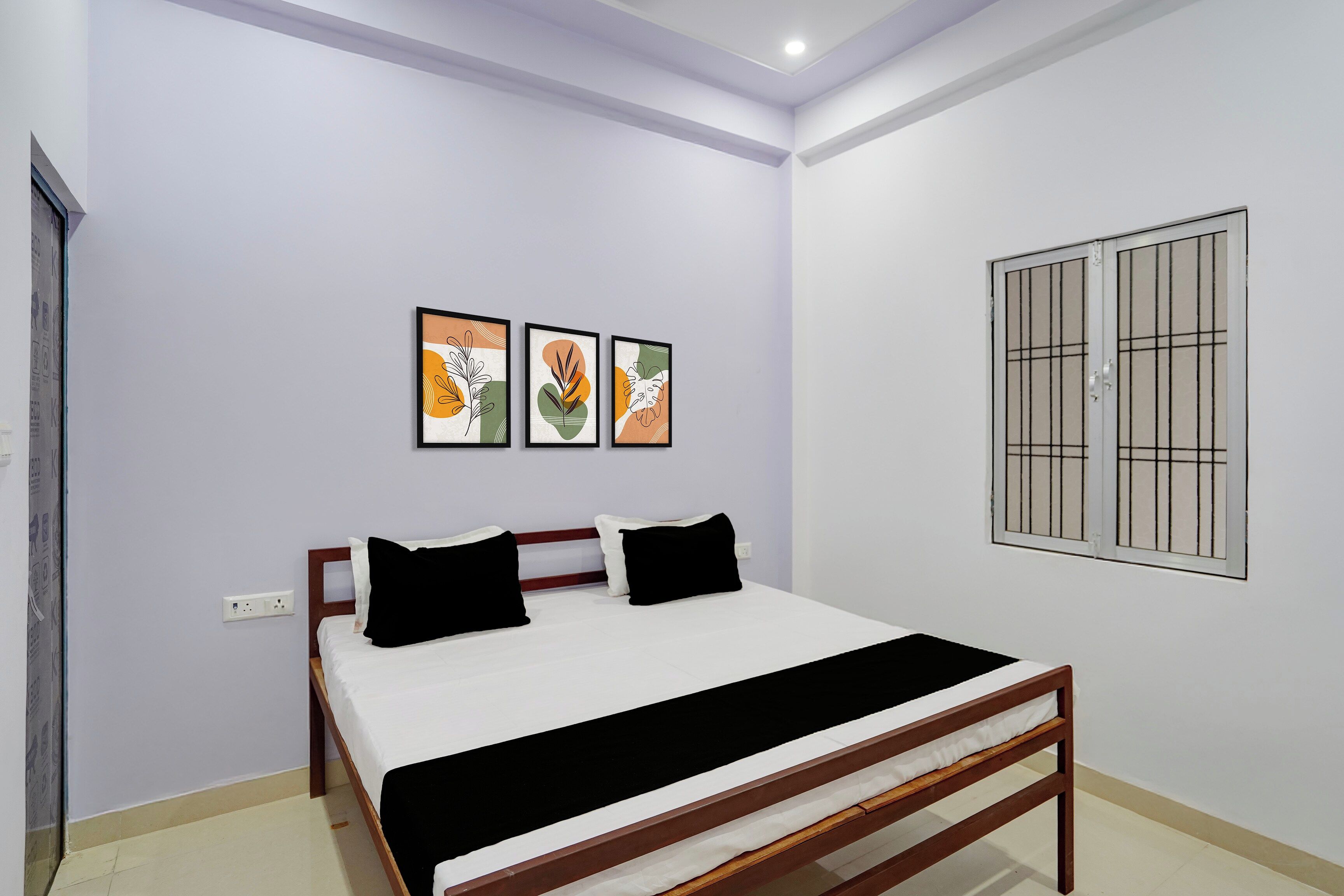 Quarto com cama, janela com grades e três obras de arte emolduradas na parede.