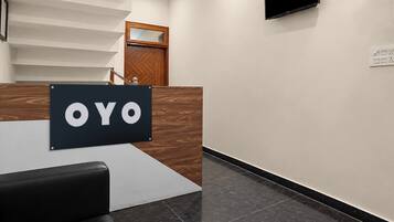 Uma receção com uma placa a indicar 'OYO' num hall moderno de hotel, com uma escadaria e uma televisão de ecrã plano na parede.