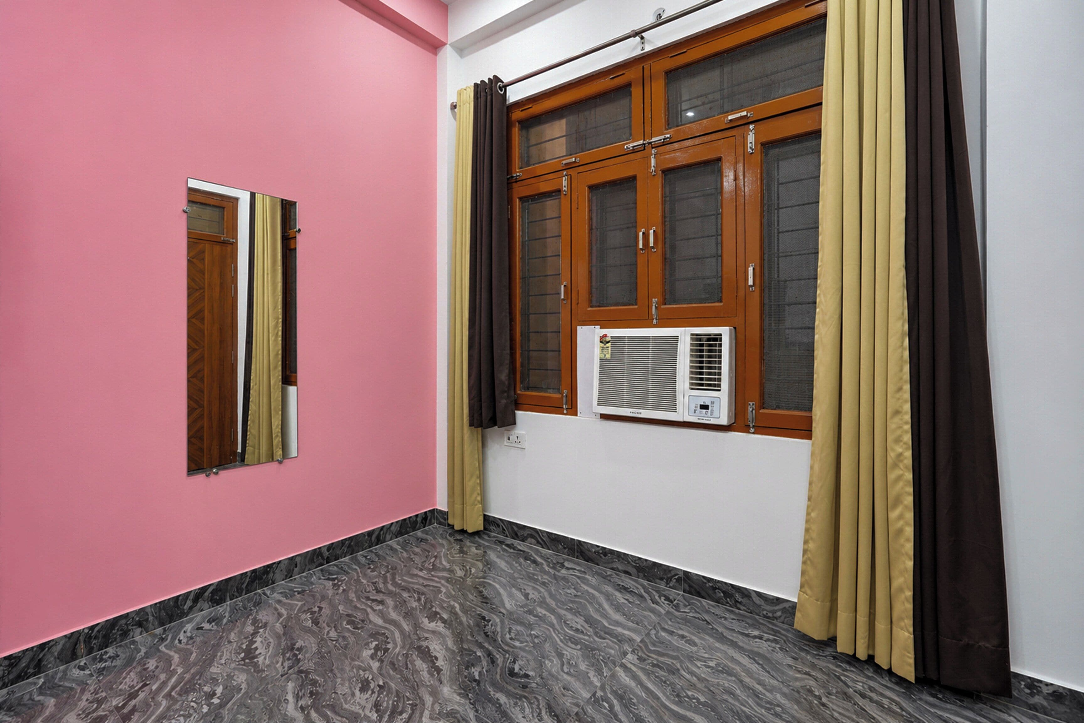 Quarto com paredes cor-de-rosa, janela com cortinas marrons, ar condicionado branco e chão com padrão marmorizado.