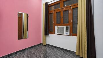 Quarto com paredes cor-de-rosa, janela com cortinas marrons, ar condicionado branco e chão com padrão marmorizado.