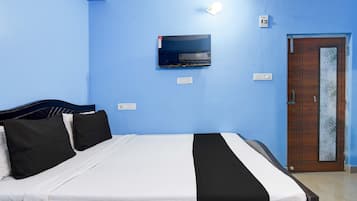 Quarto com cama, televisão fixada na parede e porta com painel de vidro jateado.