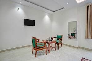Quarto de hotel com mesa de jantar, duas cadeiras, televisão de tela plana na parede e um espelho grande refletindo o ambiente.