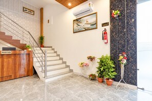 Uma área de recepção de hotel com uma escadaria de mármore, um balcão de recepção, um extintor de incêndio e um aparelho de ar condicionado fixado na parede.