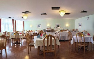 Uma sala de jantar com várias mesas e cadeiras, ventiladores de teto e luminárias fixadas na parede.