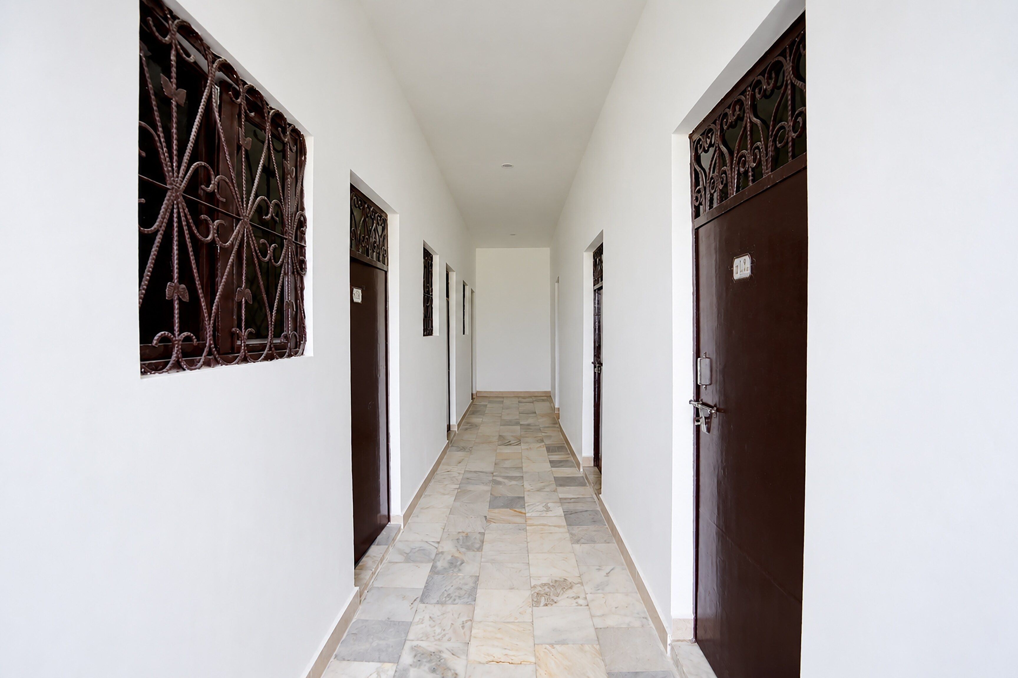 Corredor com piso ladrilhado e portas em ambos os lados, dando acesso a quartos individuais.