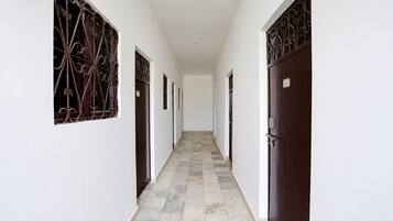 Corredor com piso ladrilhado e portas em ambos os lados, dando acesso a quartos individuais.