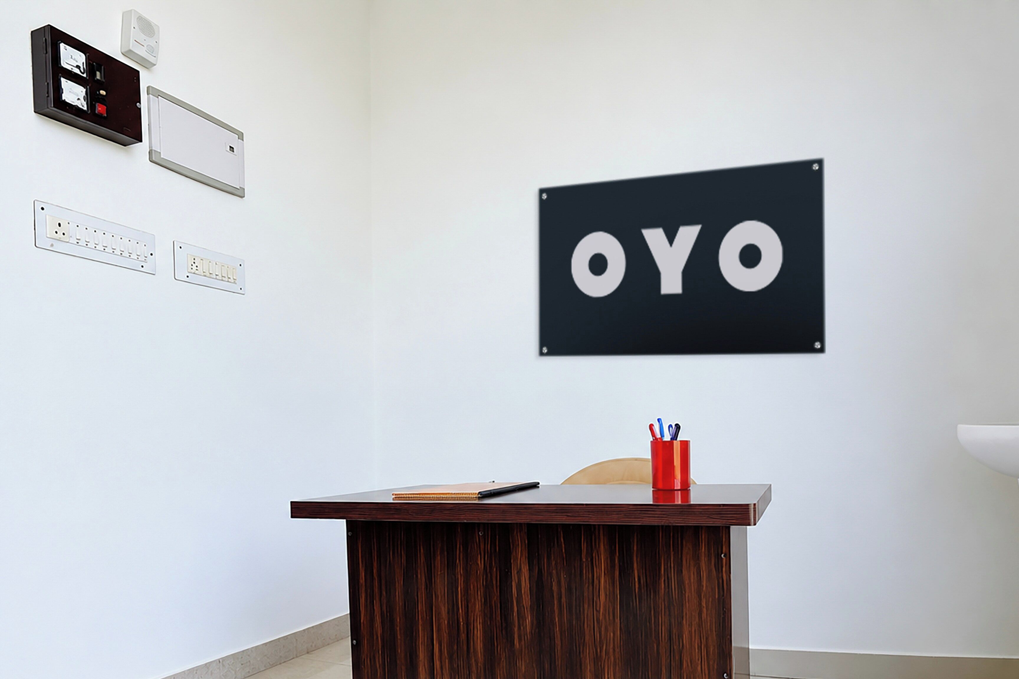 Quarto com escrivaninha, placa na parede com a inscrição 'OYO', tomadas e porta-copos vermelho.