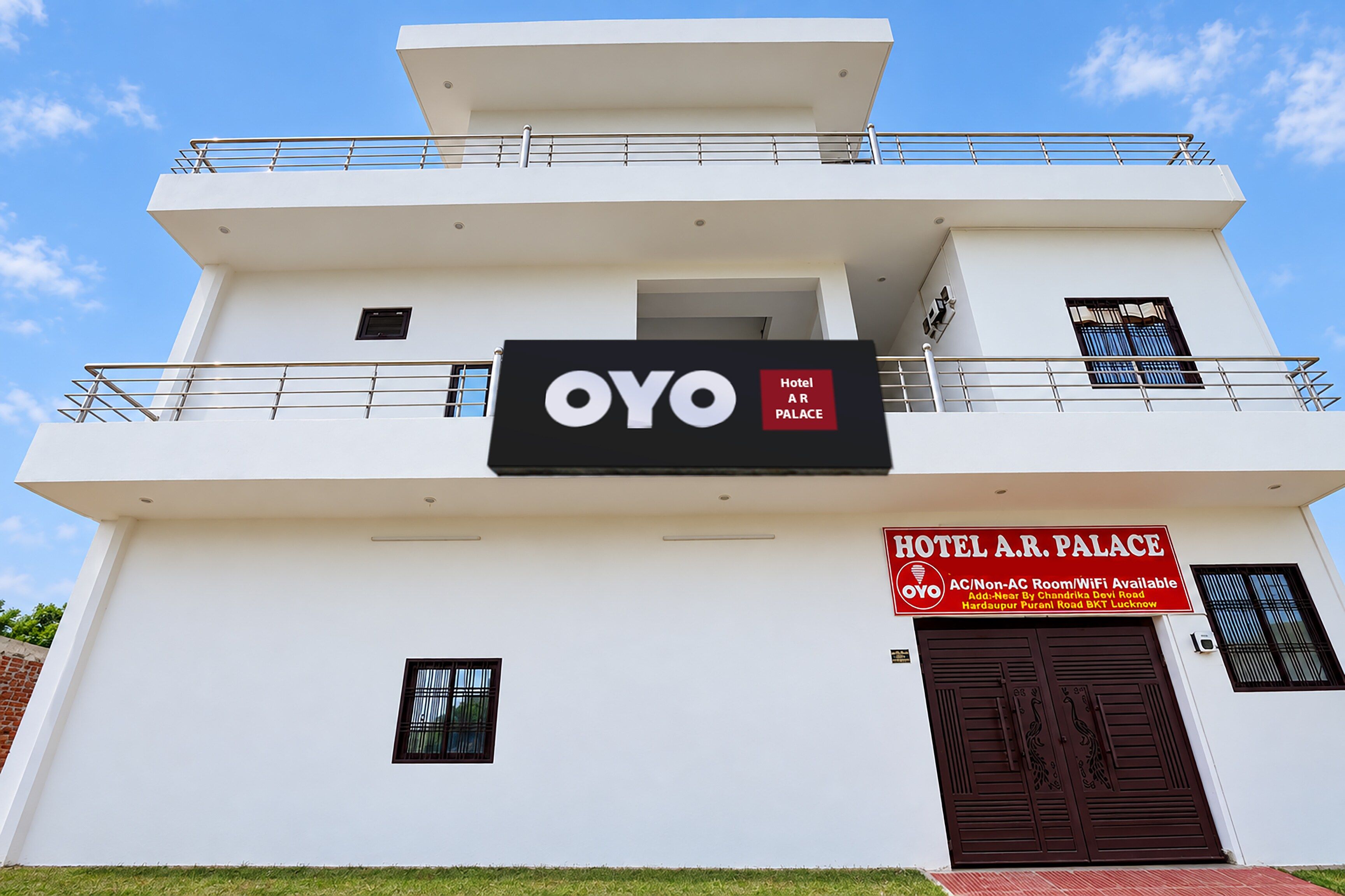Um edifício de dois andares com uma placa indicando 'OYO Hotel A.R. Palace' e outra placa que mostra 'Quarto com/sem ar condicionado/WiFi disponível'.