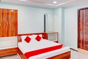 Quarto de hotel com guarda-roupa de madeira, cama com roupa de cama vermelha e branca, mesa de cabeceira e espelho.