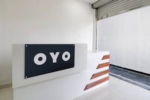 Uma placa com a palavra 'OYO' em uma parede branca, ao lado de um pilar branco com detalhes em madeira.