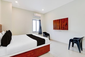 Quarto de hotel com cama, cadeira, janela com cortinas, aparelho de ar condicionado e uma obra de arte na parede.