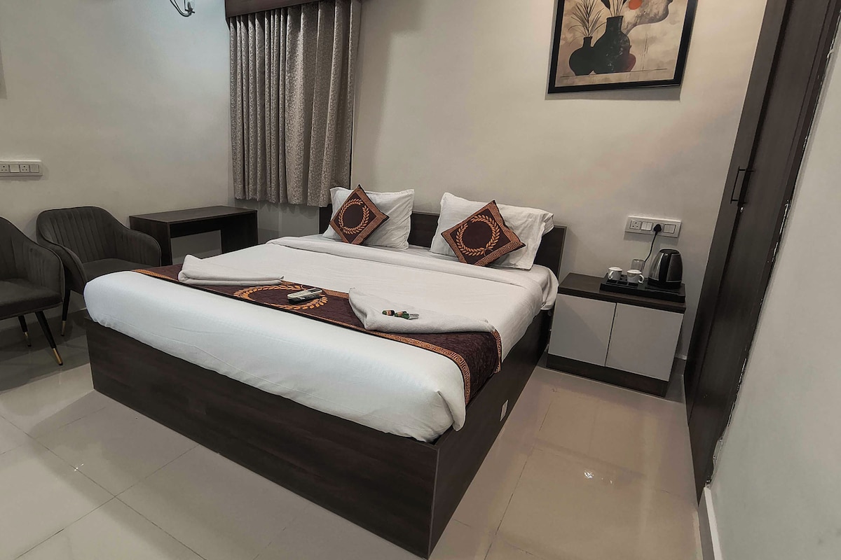 Quarto de hotel com cama, cadeira, mesa de cabeceira e um quadro na parede.