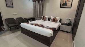 Quarto de hotel com cama, cadeira, mesa de cabeceira e um quadro na parede.
