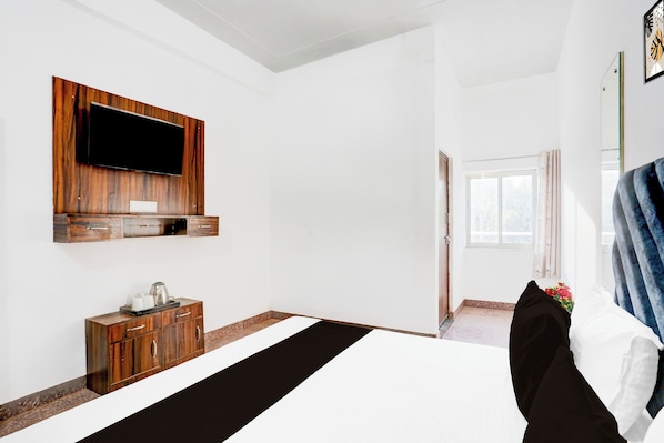 Quarto de hotel com uma cama grande, cômoda de madeira, TV de tela plana na parede e janela com cortinas.
