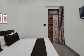 Quarto com cama, porta com cortinas estampadas e televisão presa na parede.