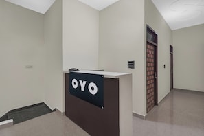 Uma receção com uma placa a indicar 'OYO' num corredor com paredes brancas e chão em mosaico.