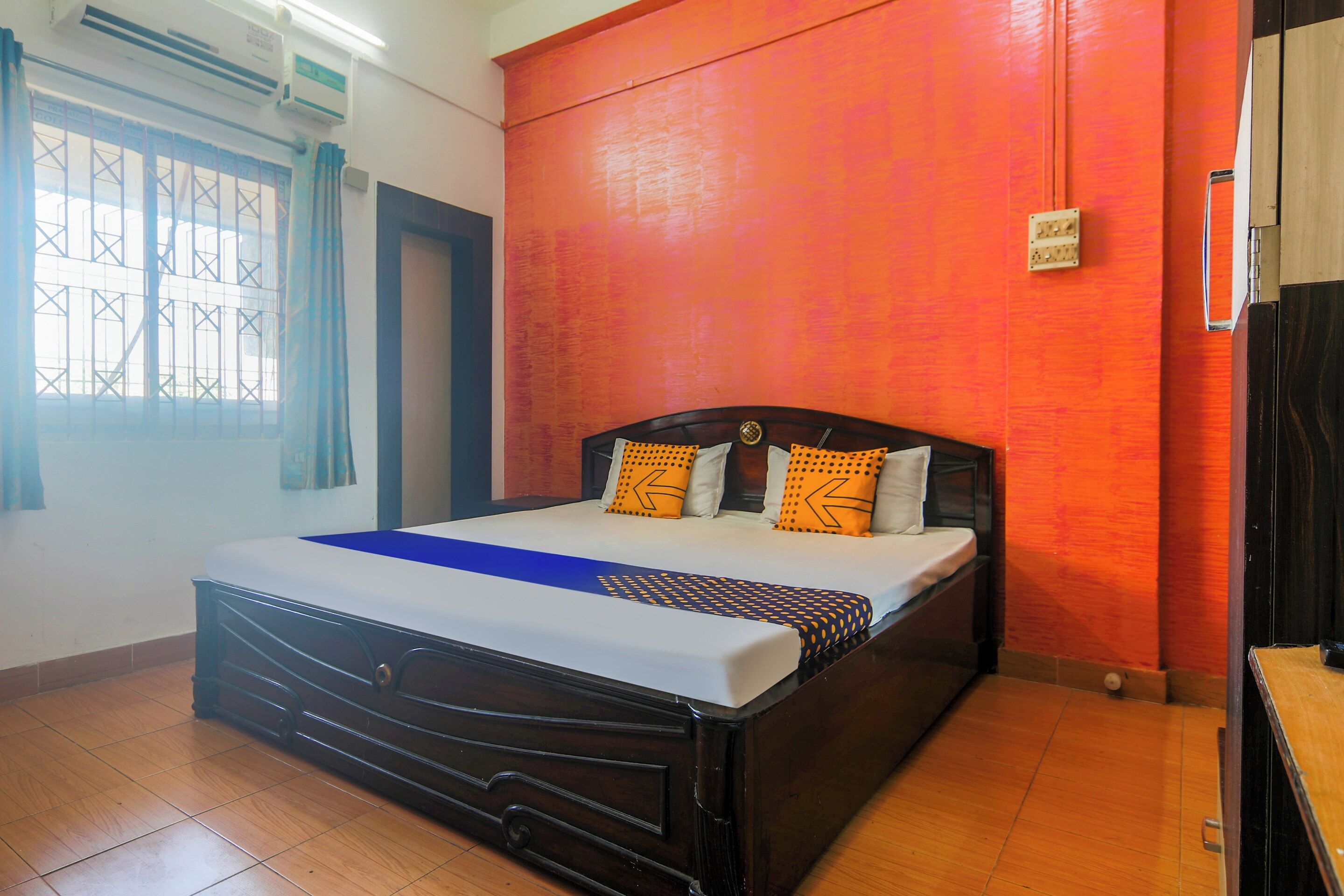 Quarto de hotel com cama, janela com cortinas e parede vermelha.