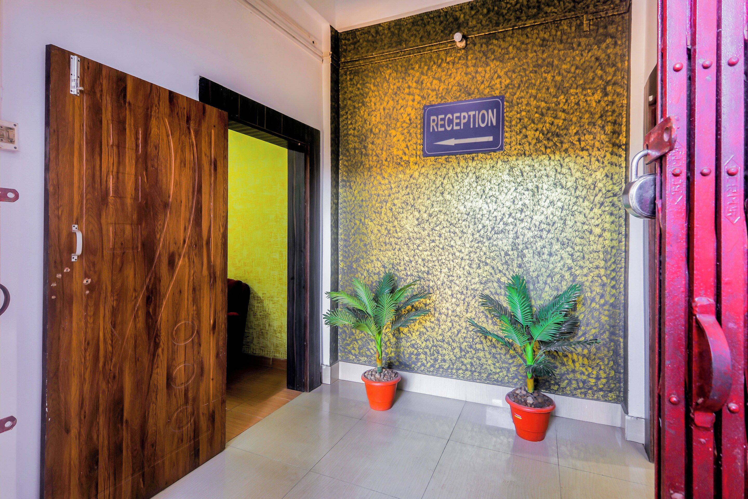 Uma área de recepção com uma placa, duas plantas em vasos e uma porta de madeira.