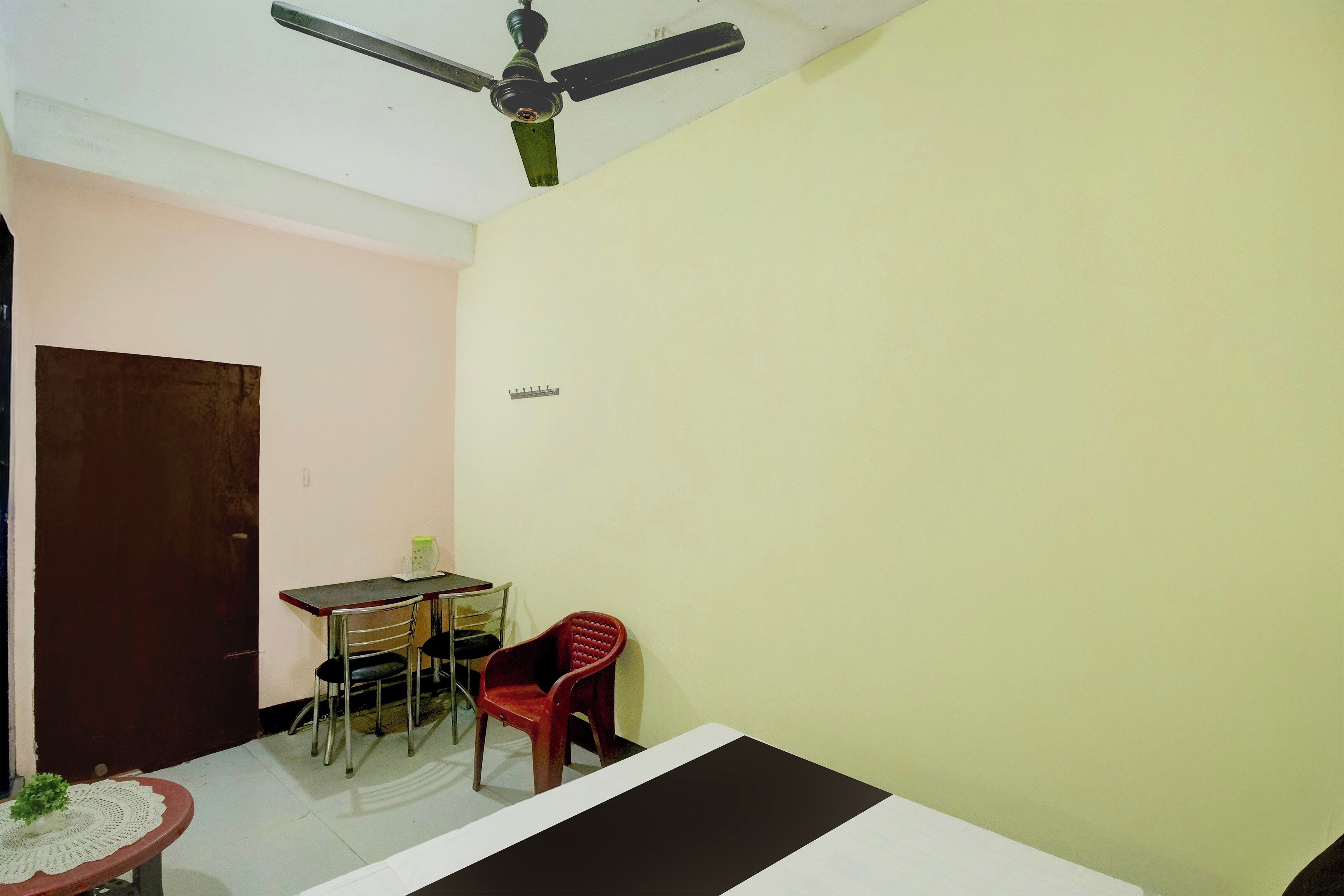 Quarto com ventilador de teto, uma mesa com cadeiras, uma porta e uma pequena planta em vaso.