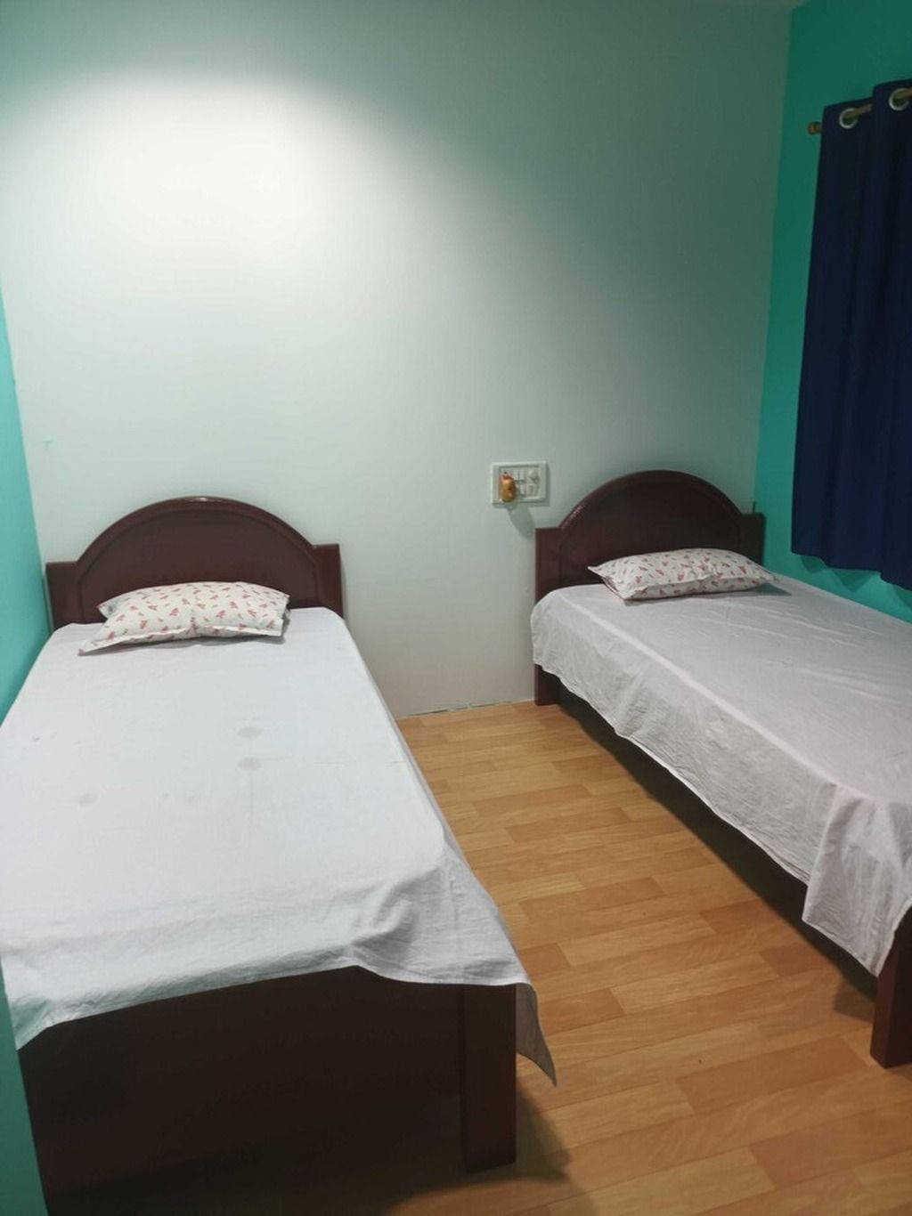 Quarto com duas camas de solteiro, cabeceiras de madeira, parede em tom claro e chão de madeira.