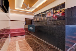 Um saguão de hotel com um sofá vermelho, uma mesa de recepção e um ventilador de teto.