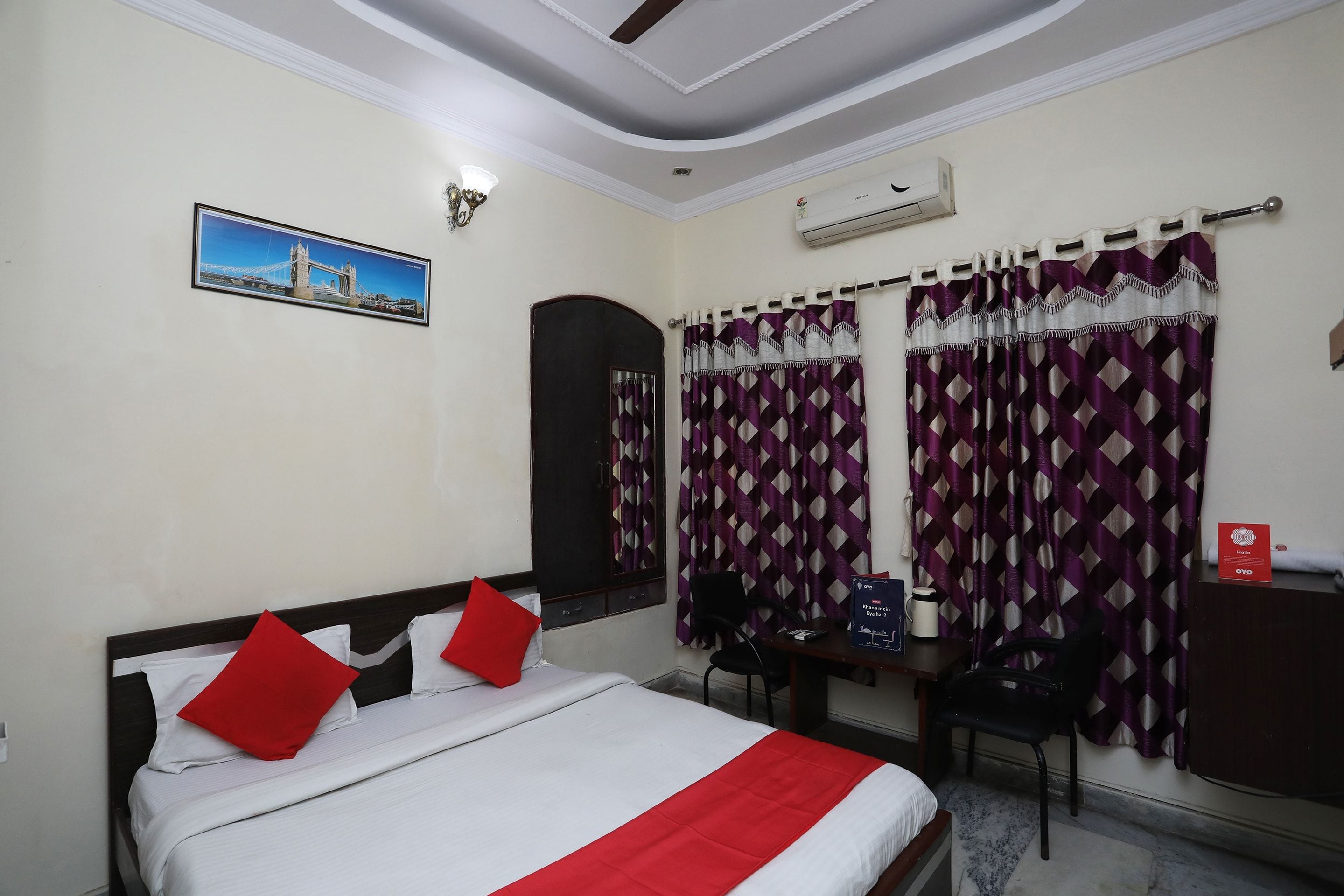 Quarto de hotel com cama, escrivaninha, cadeira, ar condicionado e cortina.
