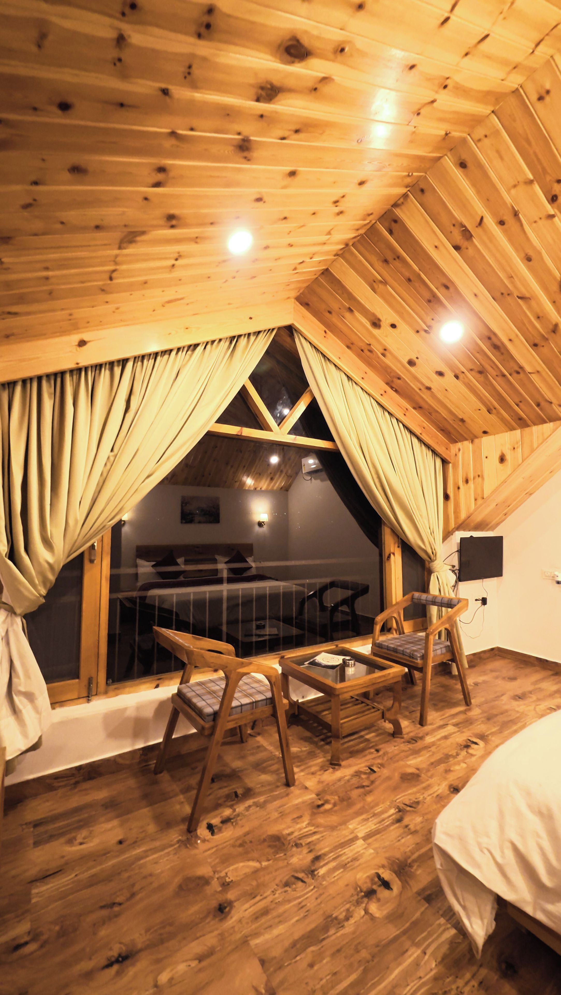 Interior de madeira com teto inclinado, divisória de vidro e uma cama.