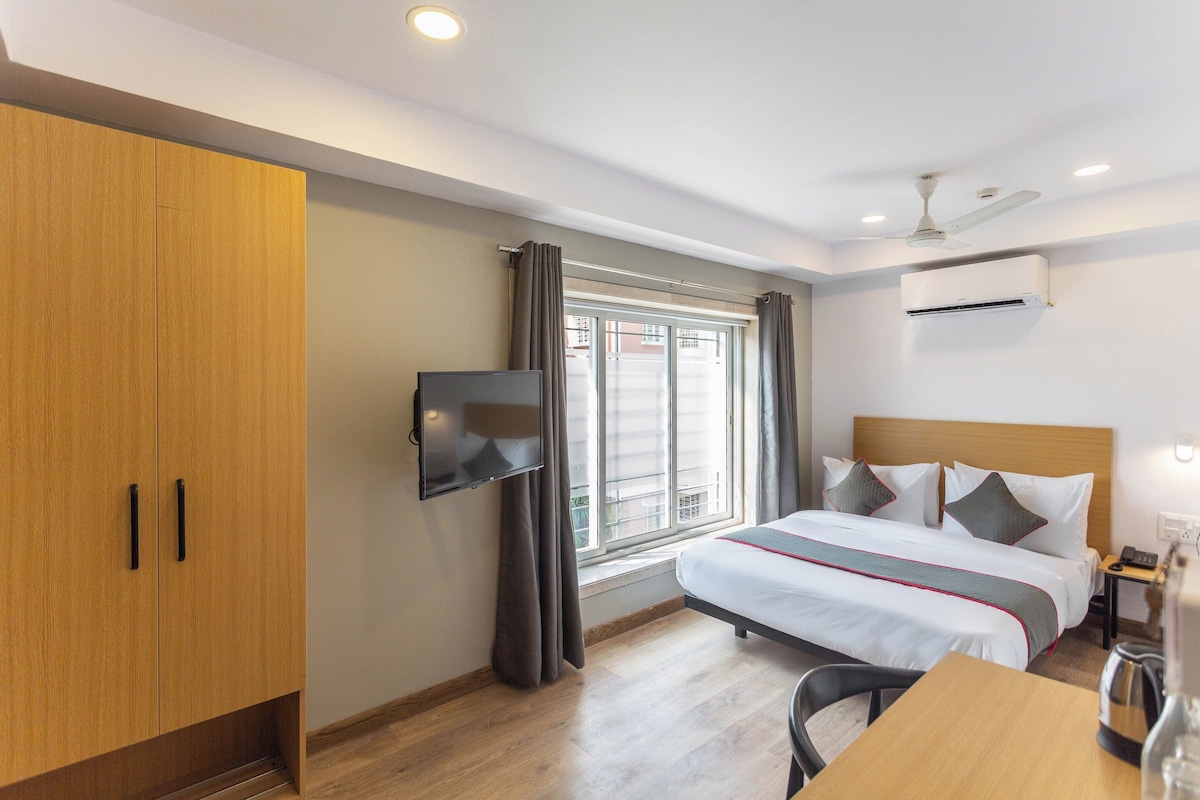 Quarto de hotel com cama, televisão, escrivaninha e guarda-roupa.