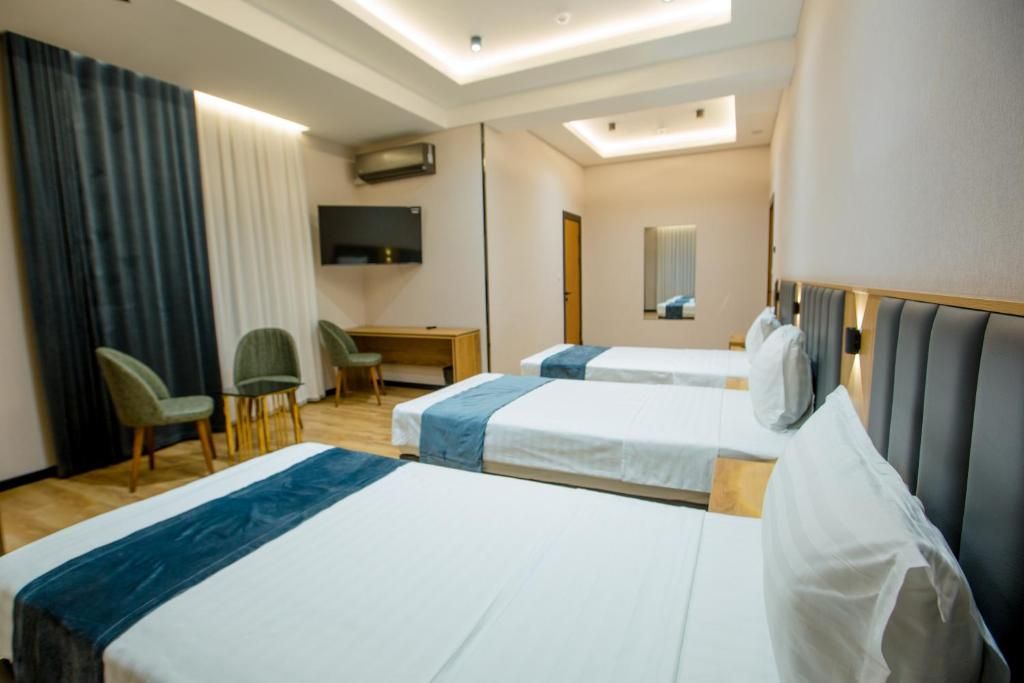 Quarto de hotel com duas camas, uma escrivaninha, uma cadeira, uma televisão e uma janela.