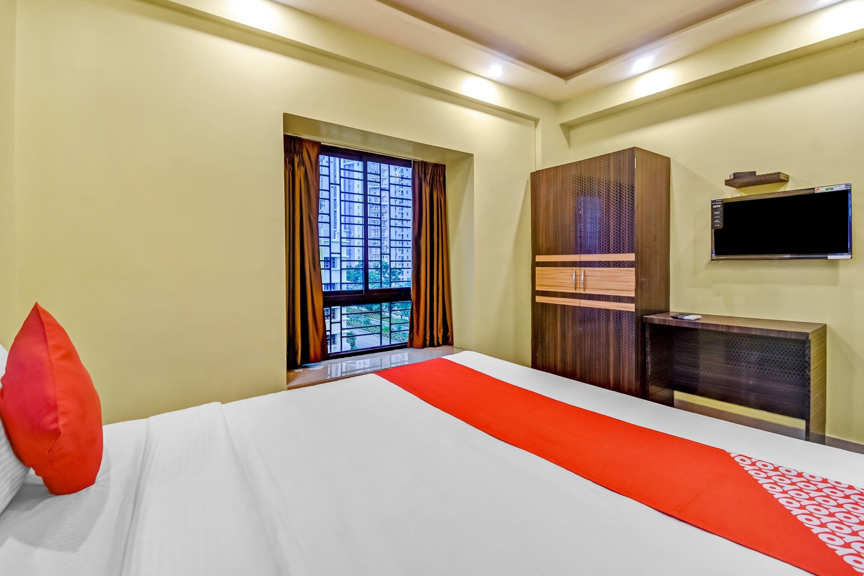 Quarto de hotel com cama, TV fixada na parede e janela com cortinas.
