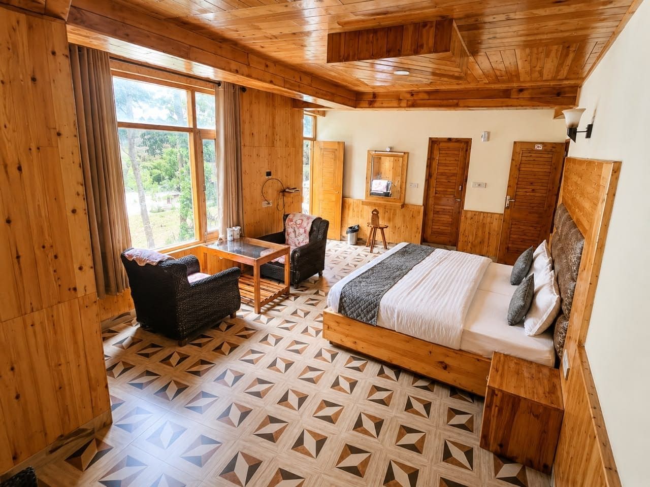 Interior de madeira com cama, duas cadeiras, uma mesa e uma janela.