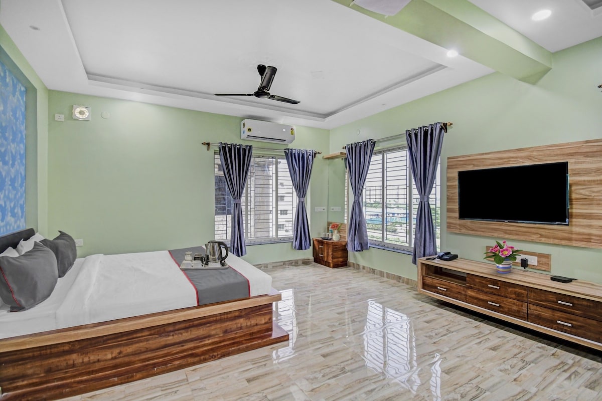 Quarto de hotel com cama, televisão, penteadeira de madeira e ventilador de teto.