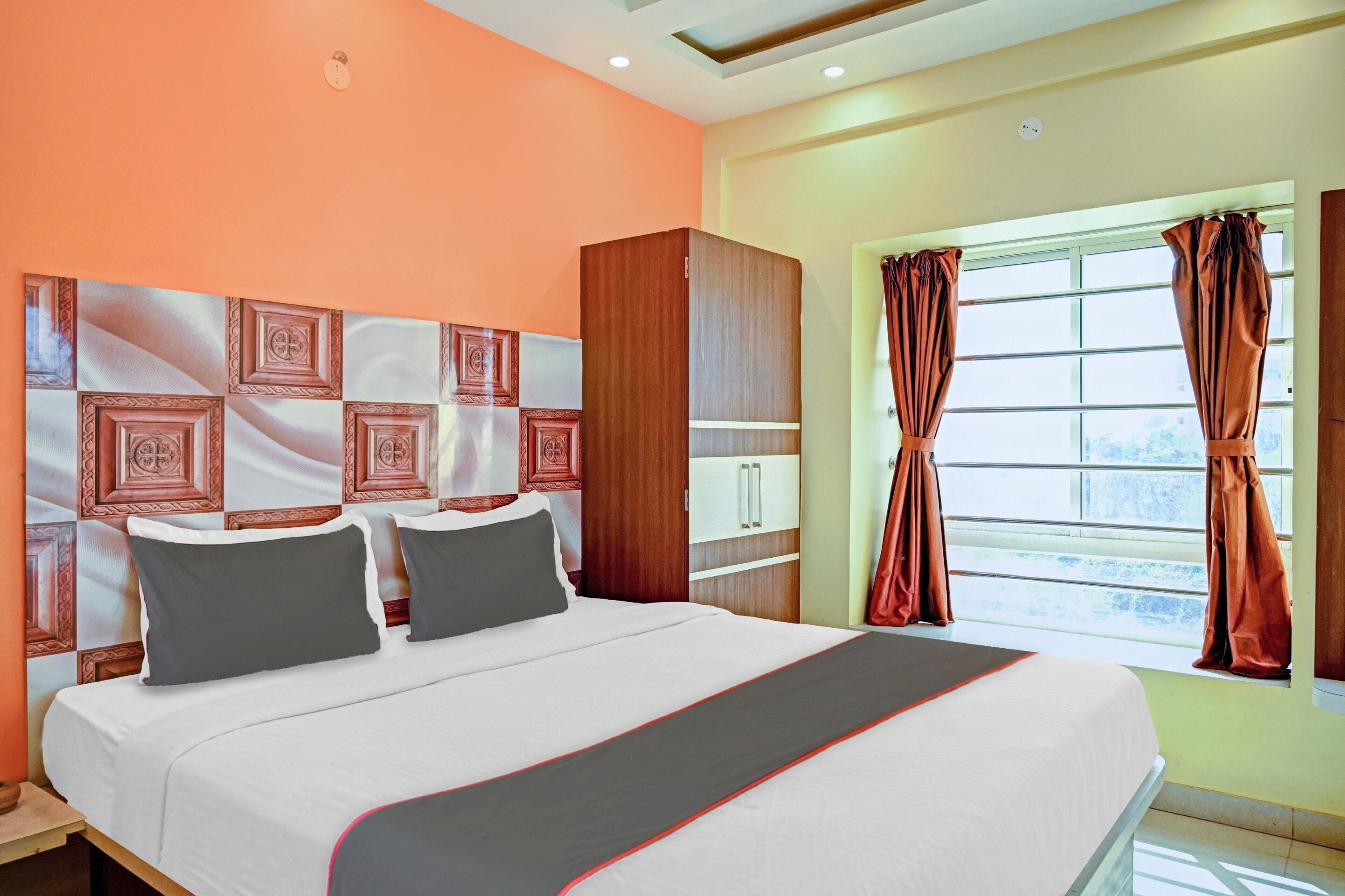 Quarto de hotel com cama, guarda-roupa, janela com cortinas e parede com um desenho estampado.