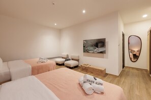 Quarto de hotel com duas camas, área de estar, espelho e quadro pendurado na parede.