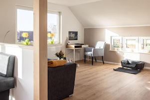 Um espaço de estar moderno com pé-direito estilo loft, área de refeições com mesa e cadeiras, e um espaço de estar aconchegante com sofá e cama para animais de estimação.