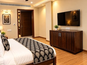 Quarto com cama, guarda-roupa, televisão e planta.