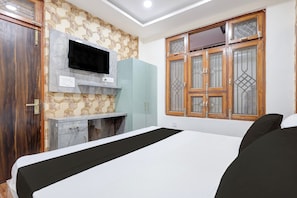 Quarto com cama, televisão presa na parede, guarda-roupa e janela com molduras de madeira.