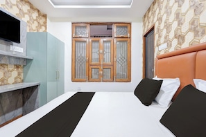 Quarto de hotel com cama, televisão na parede, guarda-roupa e janela com moldura de madeira decorativa.