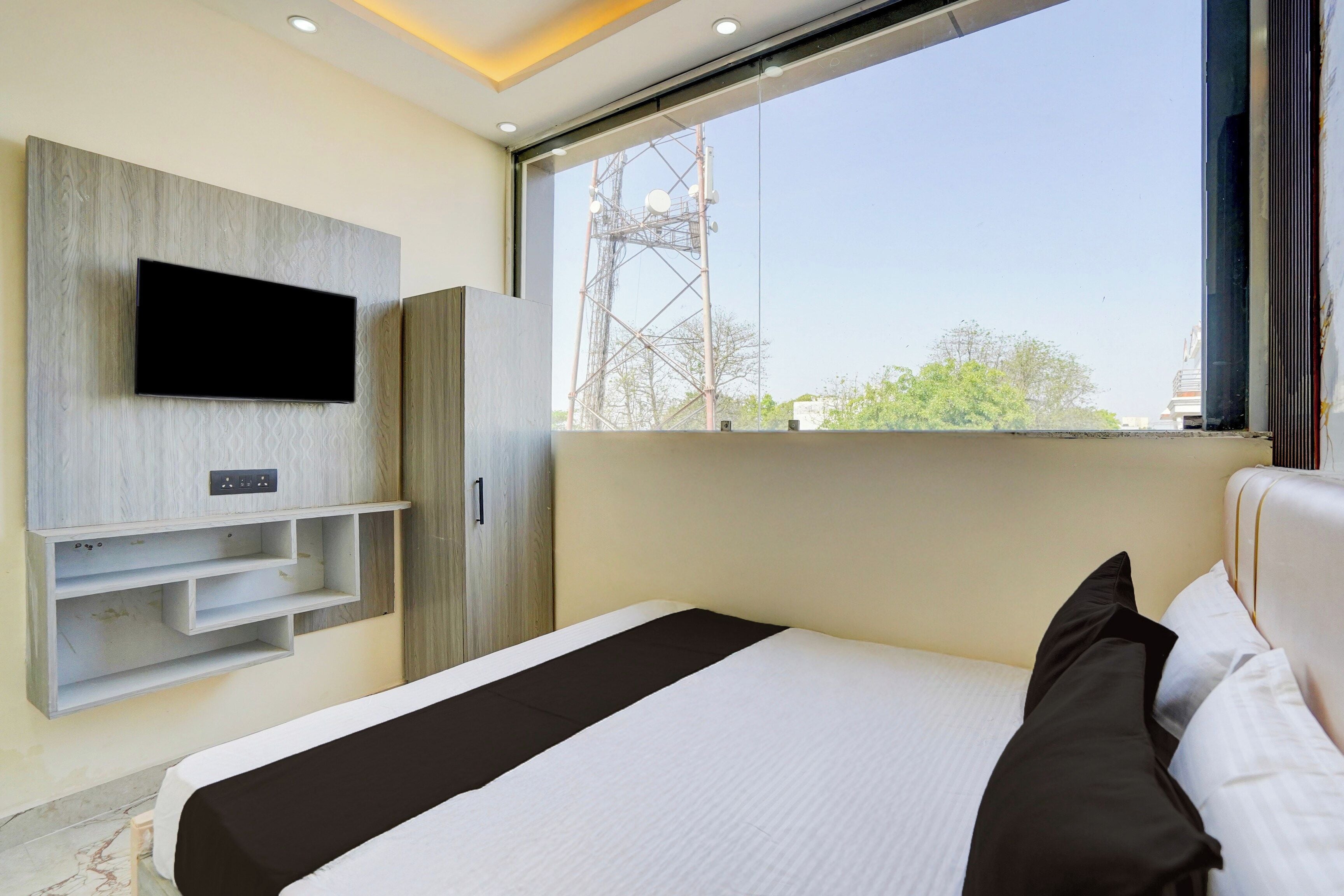 Quarto de hotel moderno com uma cama grande, uma TV de tela plana fixada em um painel de madeira e uma janela com vista para o exterior.
