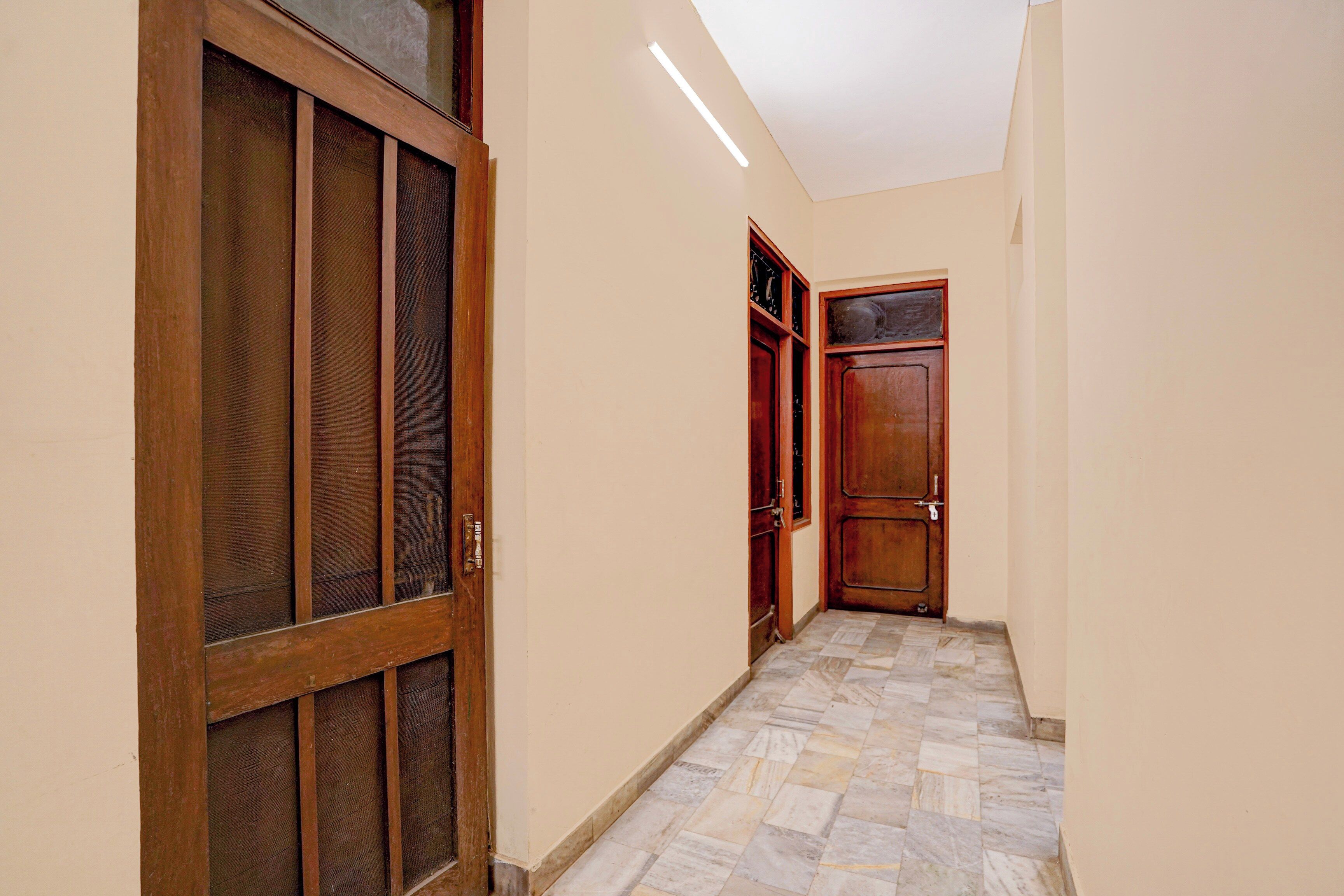 Corredor com porta de madeira à esquerda, guarda-roupa com espelho e chão em azulejo.
