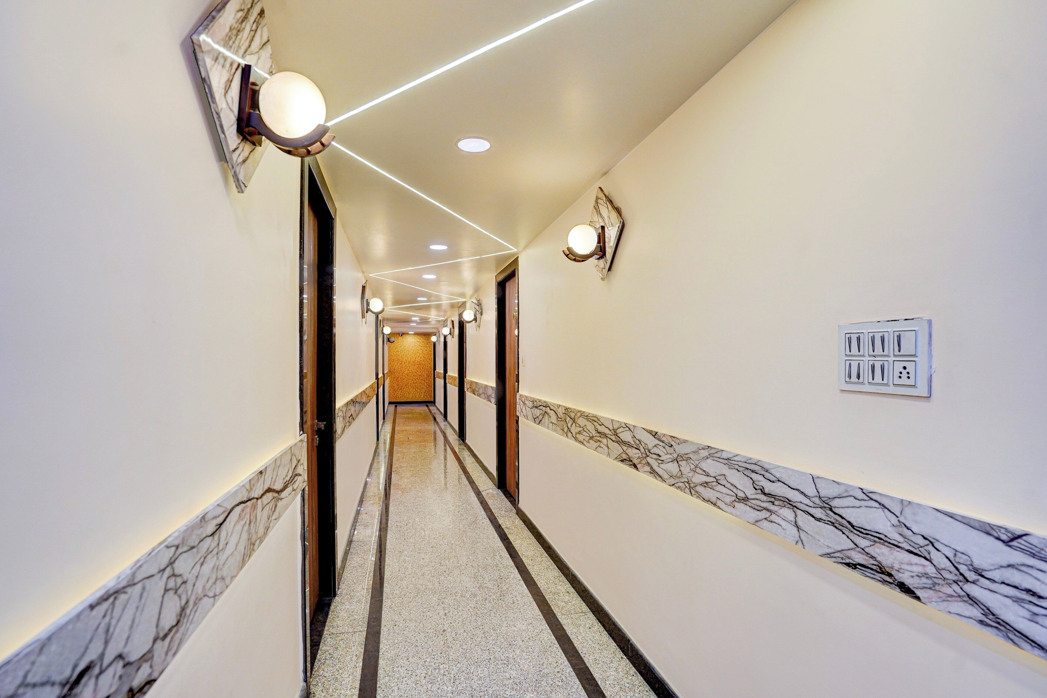 Corredor de hotel com piso de mármore, iluminação embutida e luminária na parede.