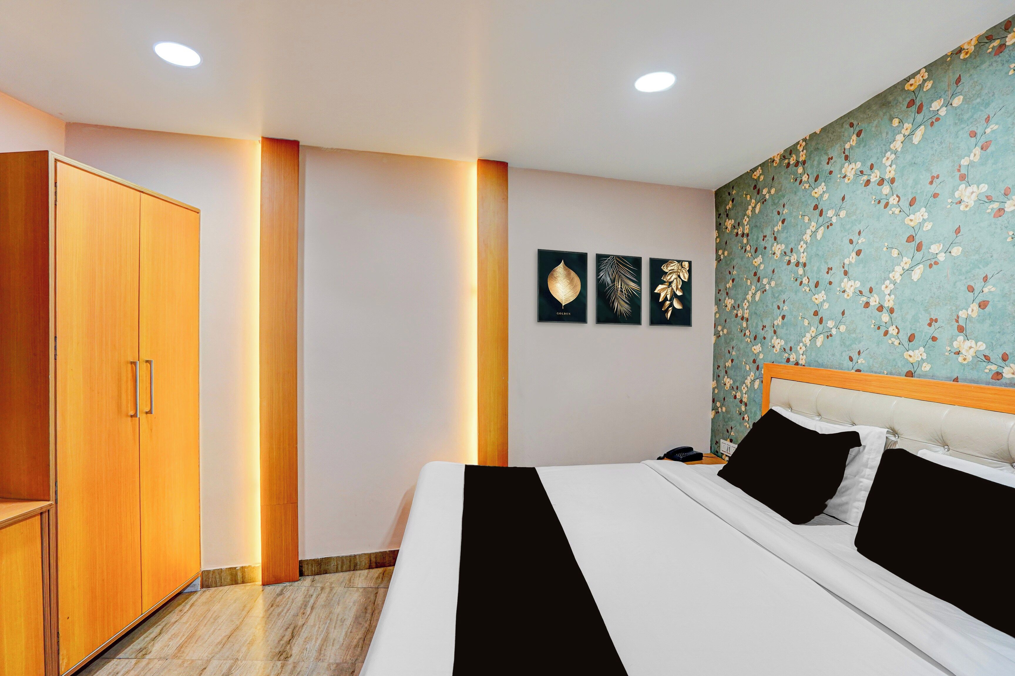 Quarto de hotel com cama, guarda-roupa e parede decorada com três gravuras de plantas.