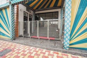 Entrada protegida por grades, com toldo estampado, câmera de segurança e piso de azulejos.