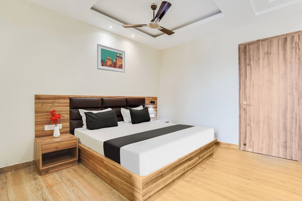 Quarto moderno com cabeceira de madeira, cama com roupa de cama preta e branca, mesa de cabeceira com um vaso e ventilador de teto.