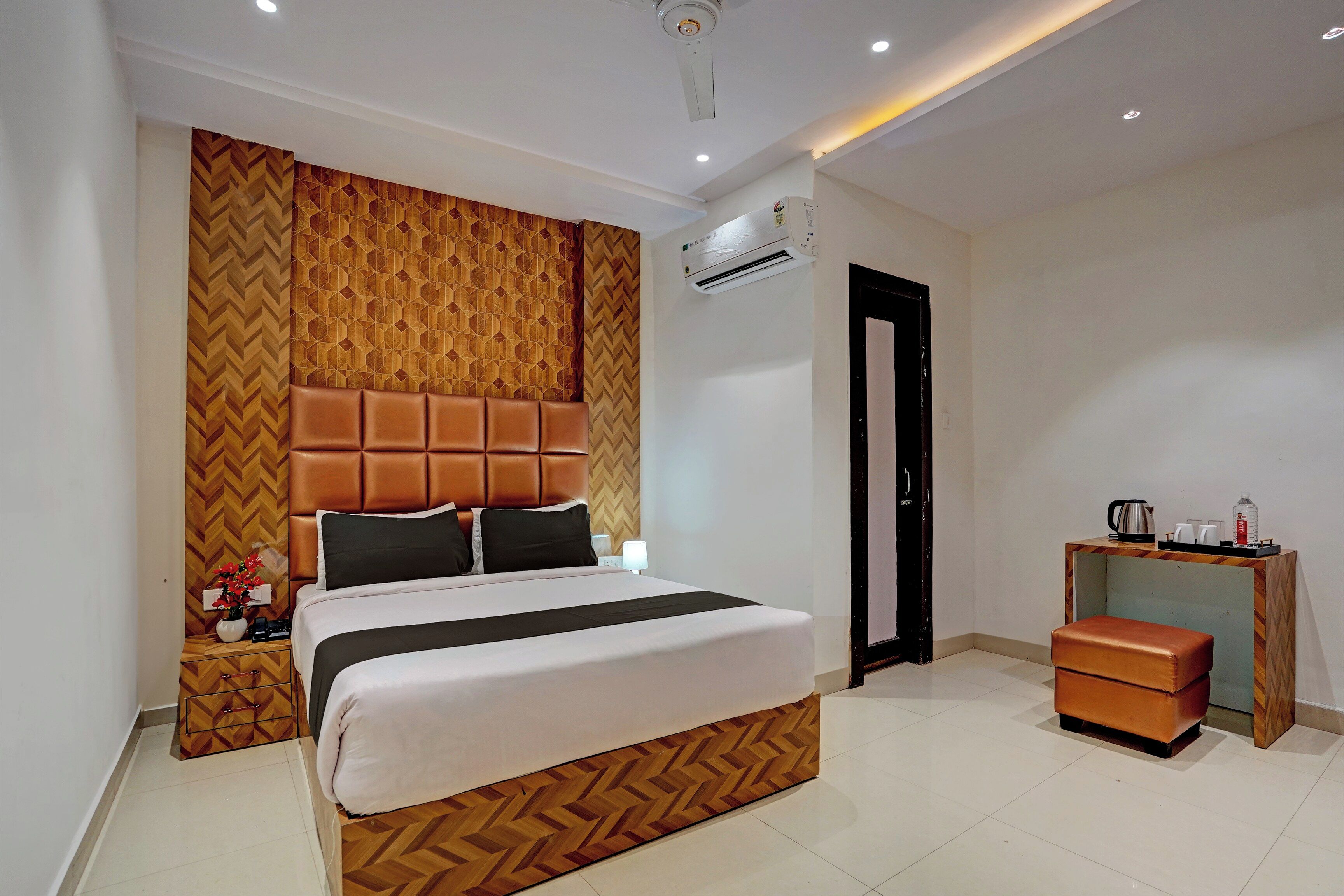 Quarto de hotel com uma cama grande, cômoda, escrivaninha com chaleira e ar condicionado.