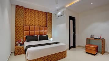 Quarto de hotel com uma cama grande, cômoda, escrivaninha com chaleira e ar condicionado.