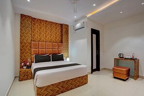 Quarto de hotel com uma cama grande, cômoda, escrivaninha com chaleira e ar condicionado.